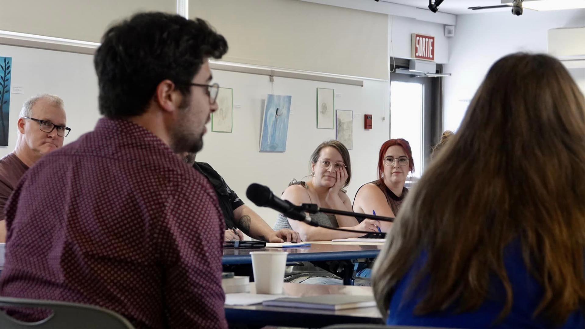 A man is speaking into a microphone. The audience in the background is ...