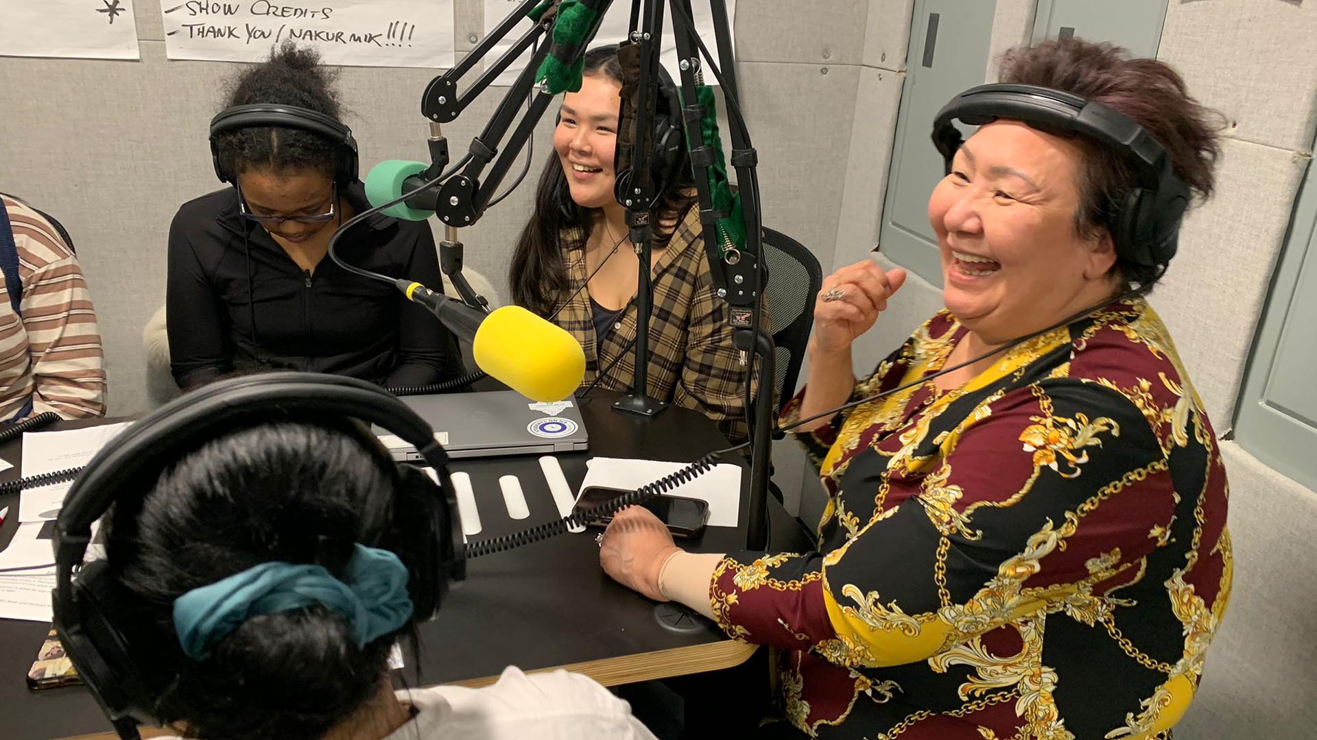 A group of four women are sitting around the table in a radio studio ...