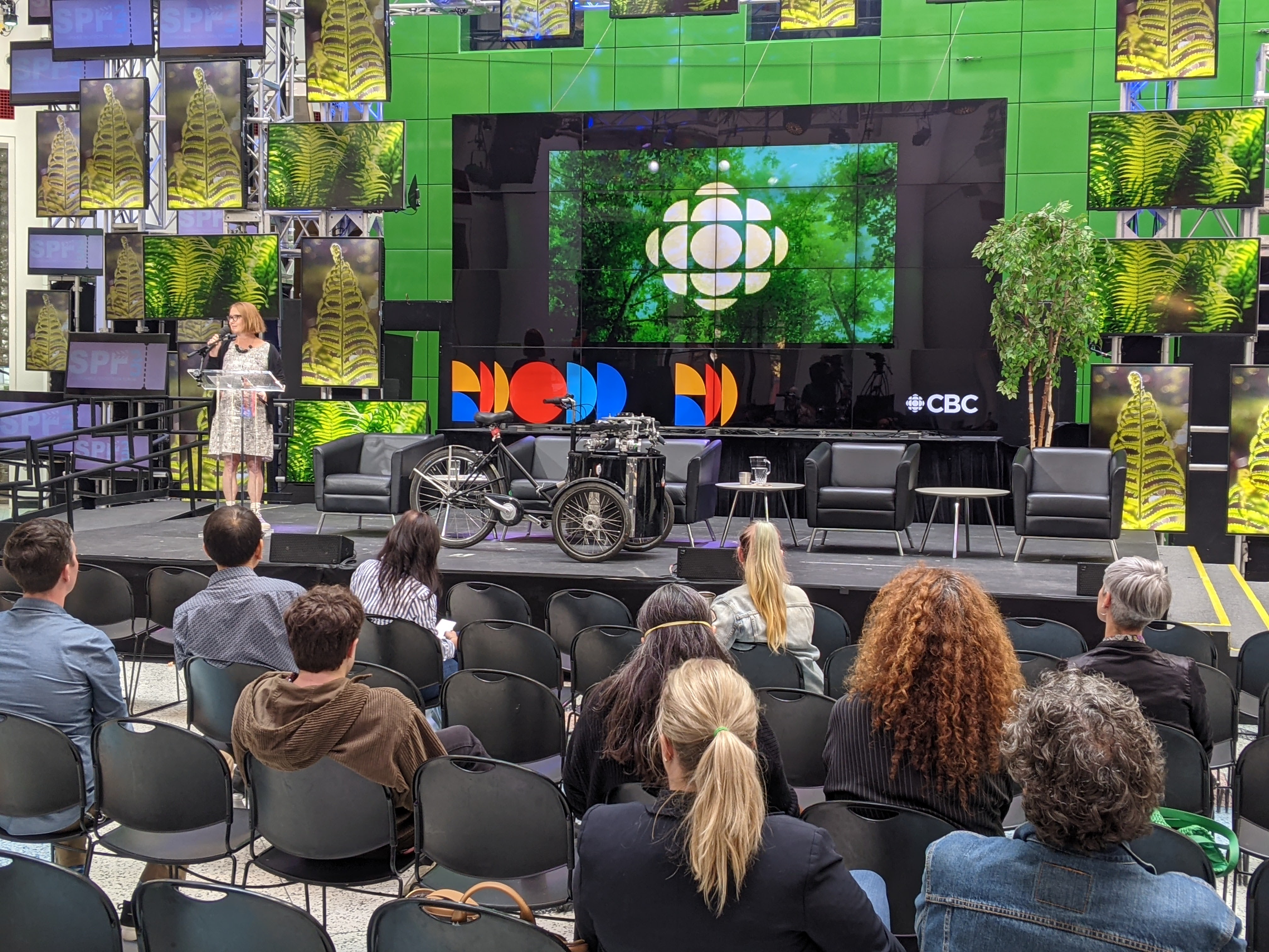 Une présentatrice sur scène s'adresse à l'auditoire. Le décor est ...