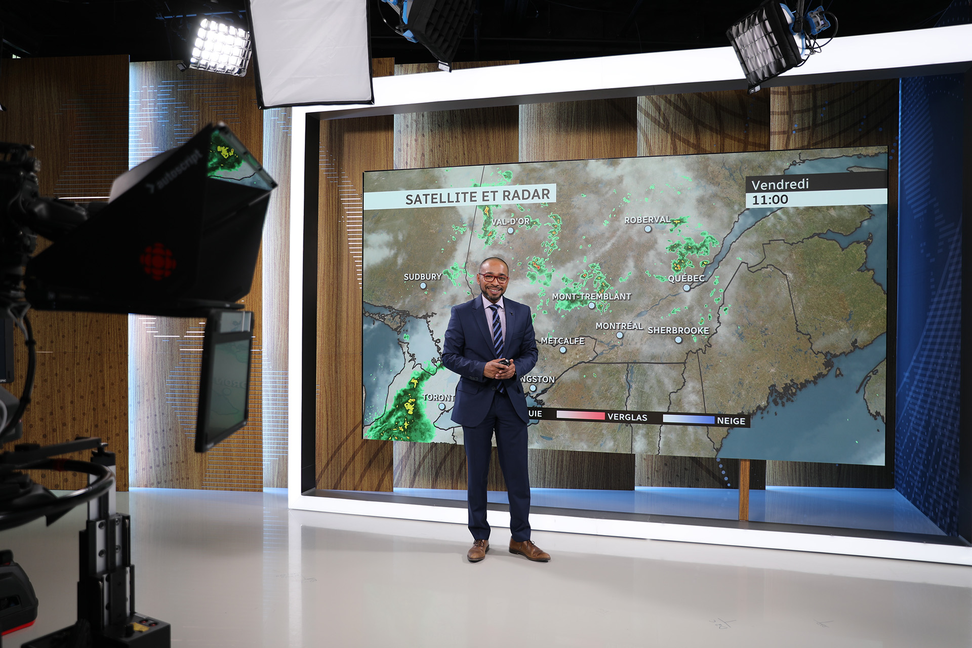 Waldir Da Cruz portant un costume bleu debout dans le studio météo devant une grande carte météo