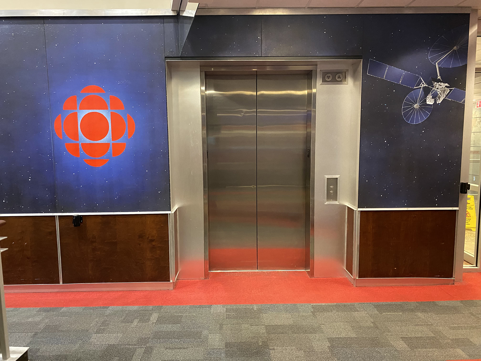 Newsroom elevator with blue walls decorated with a red gem and a satellite on the right