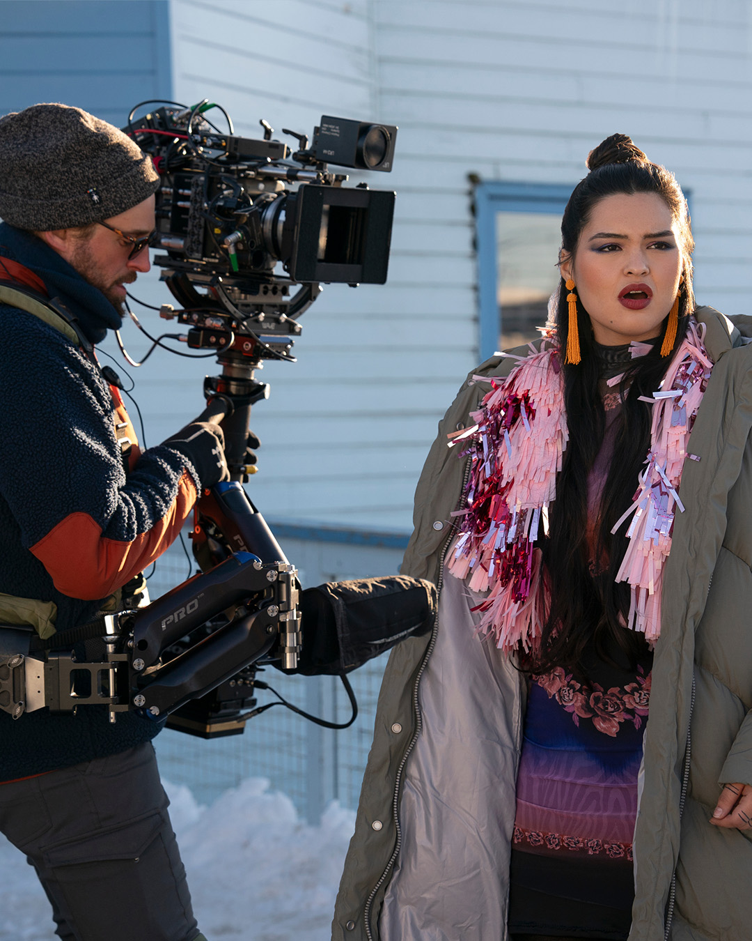 A woman wearing a coat and scarf stands beside a camera and a cameraman ...