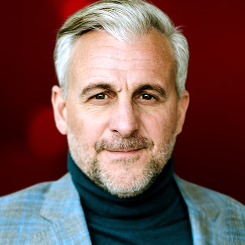 Patrick Huard wearing a blue patterend jacket and black turtleneck