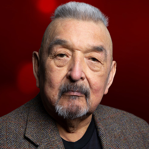 Graham Greene wearing a brown jacket and black shirt