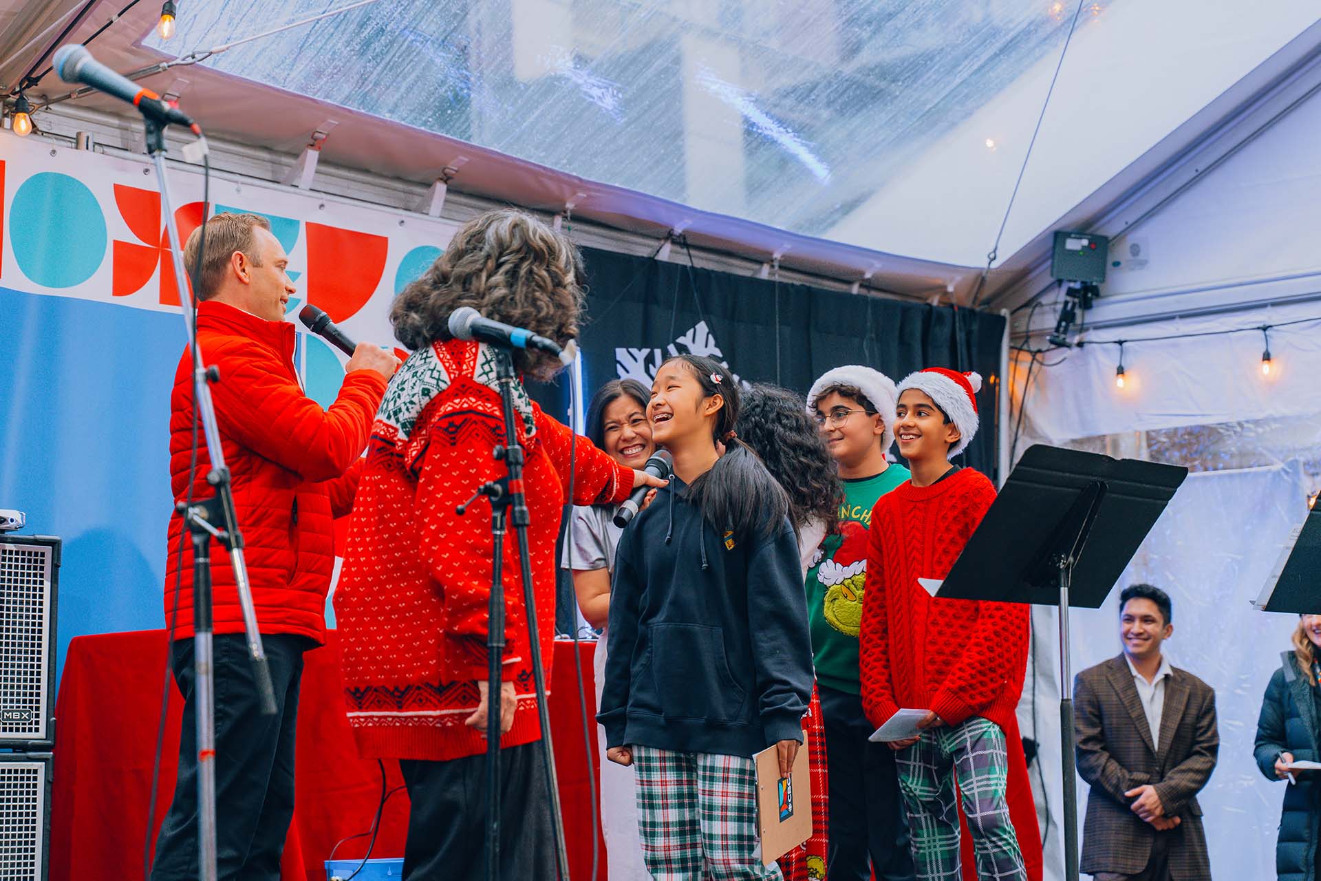 A group of youth are shown on stage smiling with a woman and CBC host.